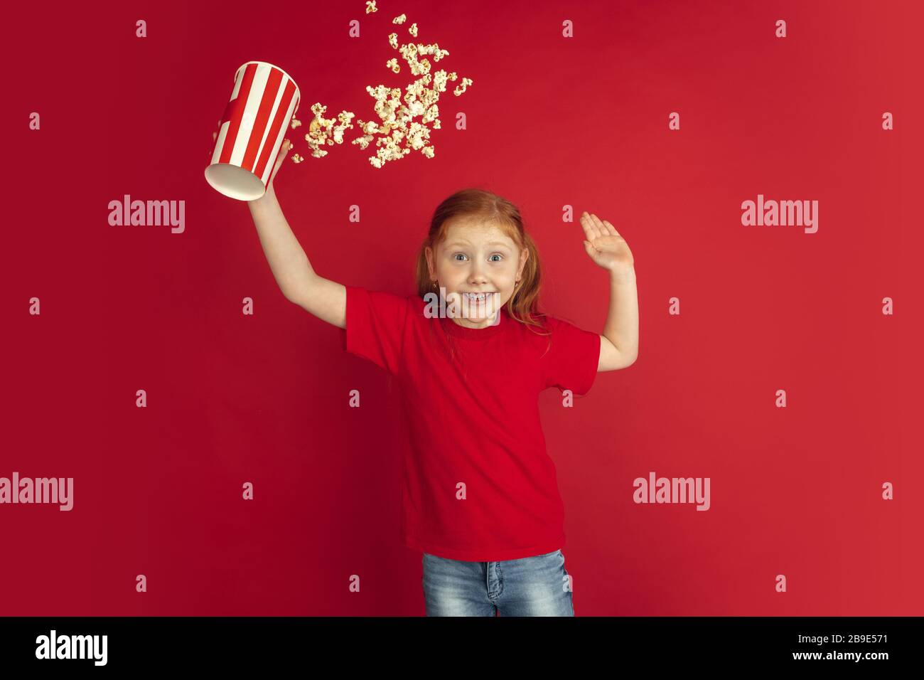 Crazy happy, flying popcorn. Caucasian little girl portrait on red ...