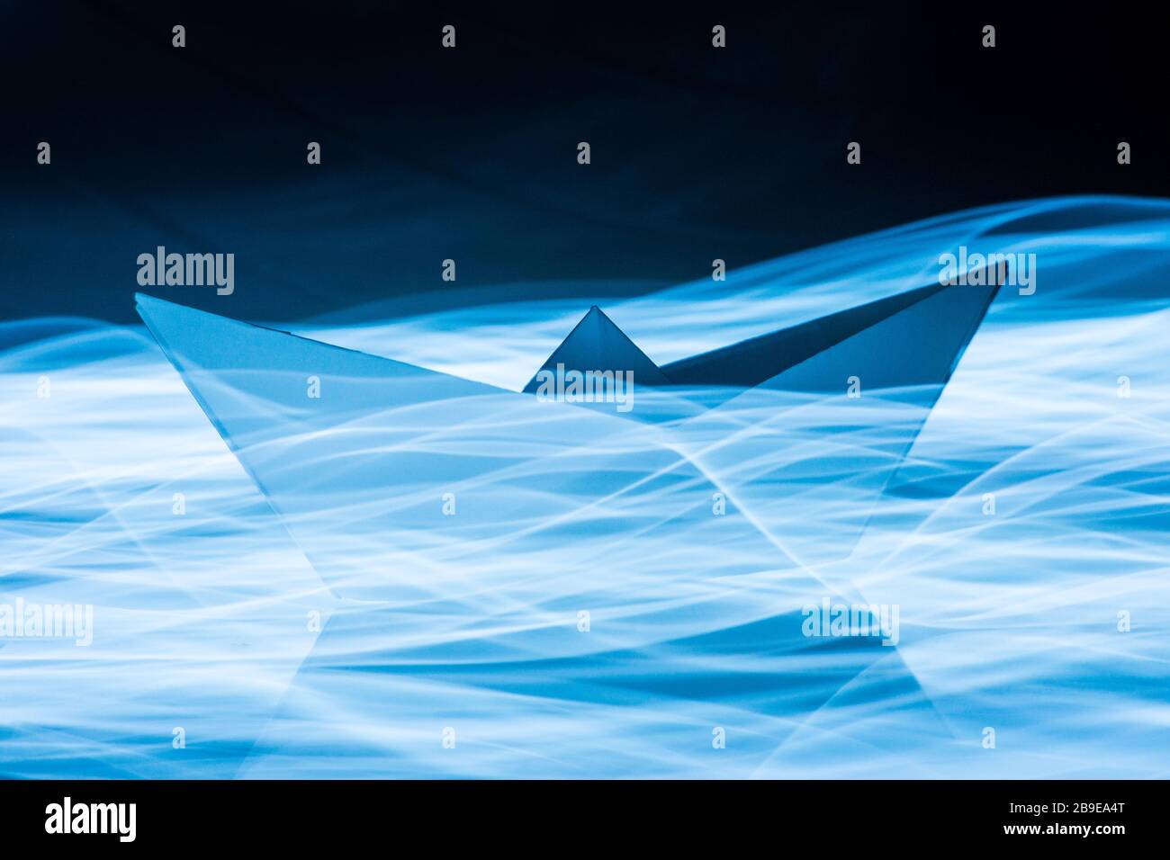 Paper boat splitting blue light trails symbolizing waves in the sea ...