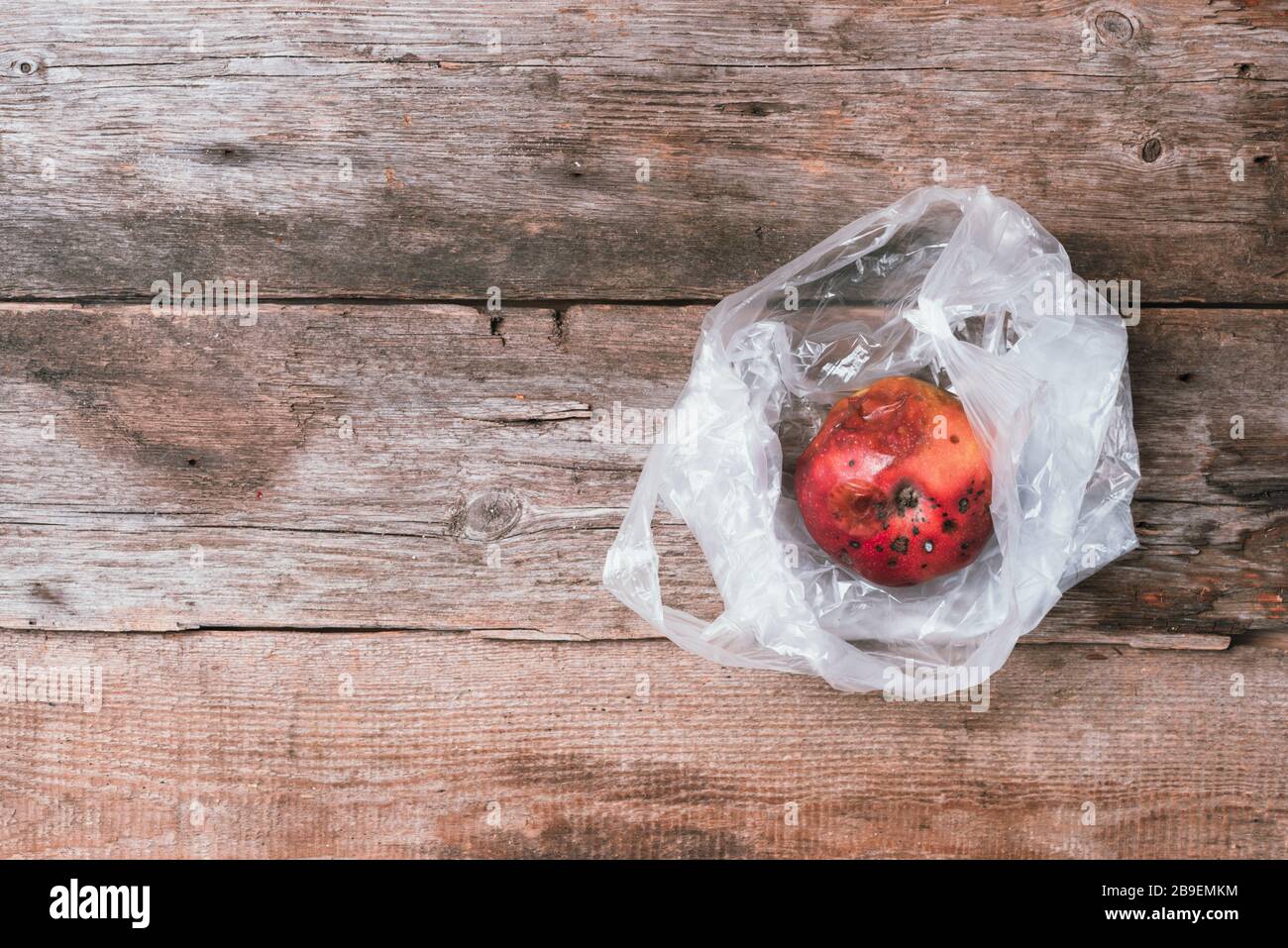 Spoiled bad red apple in plastic bag on wooden background. Garbage dump ...