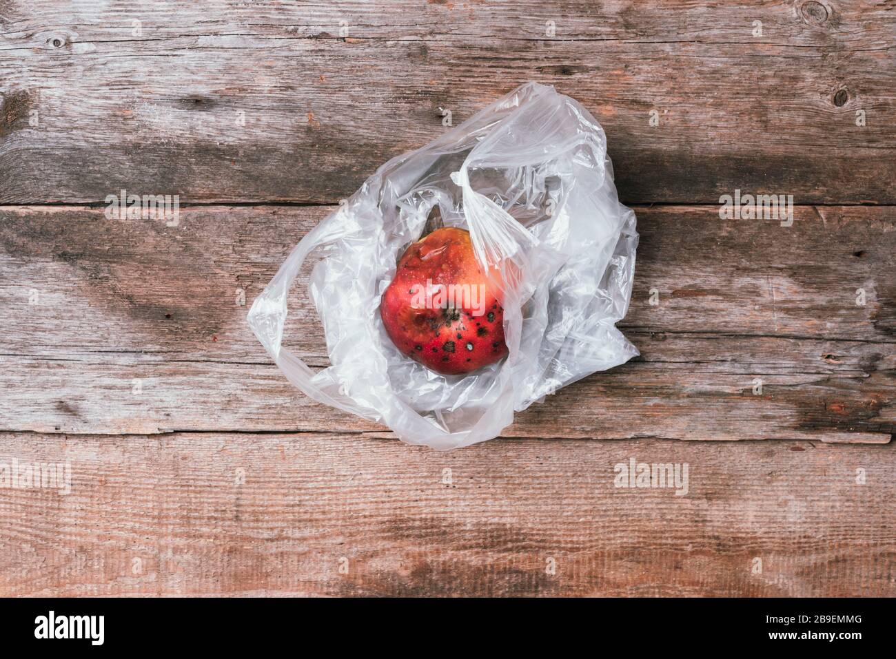 Spoiled bad red apple in plastic bag on wooden background. Garbage dump ...
