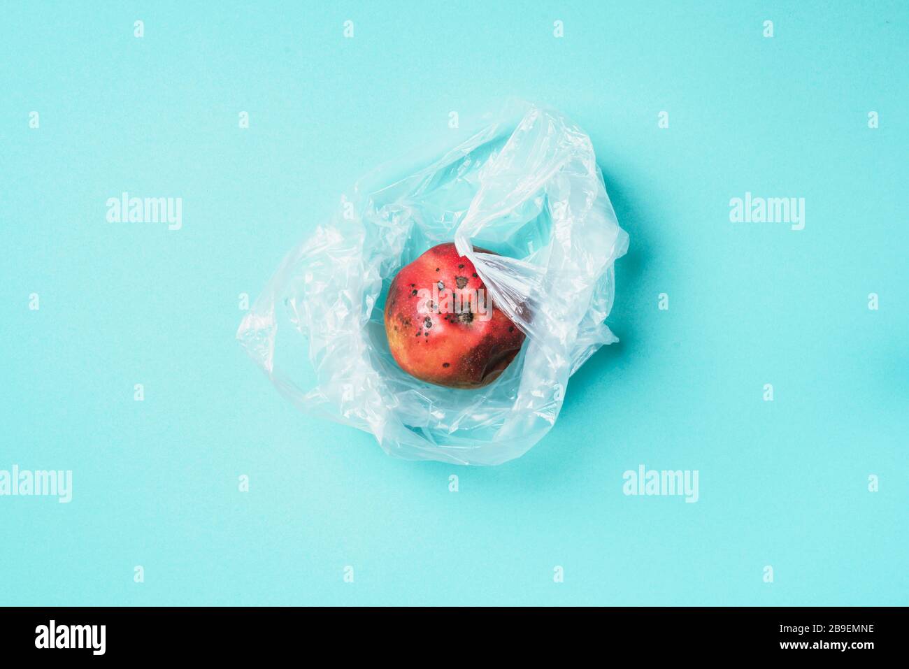 Spoiled bad red apple in plastic bag on blue background. Garbage dump ...