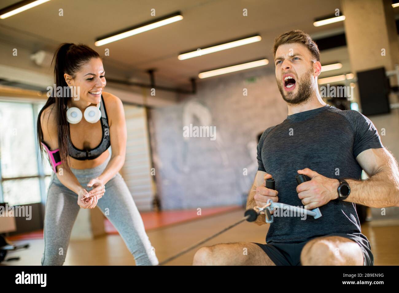 Handsome young man using seated row machine in the gym with support of ...