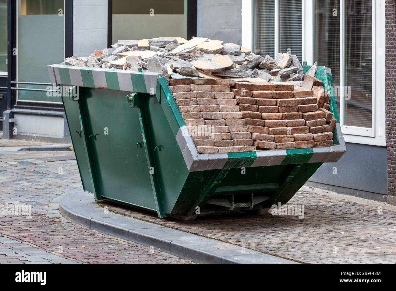Neat industrial skip parked on the clean sidewalk full loaded with ...