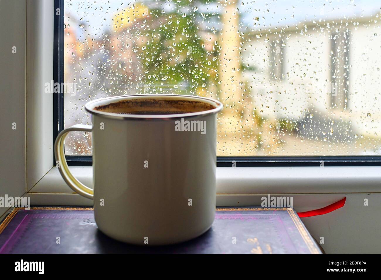 Coffee mug on a rainy day window background. Metal mug on pile of books ...