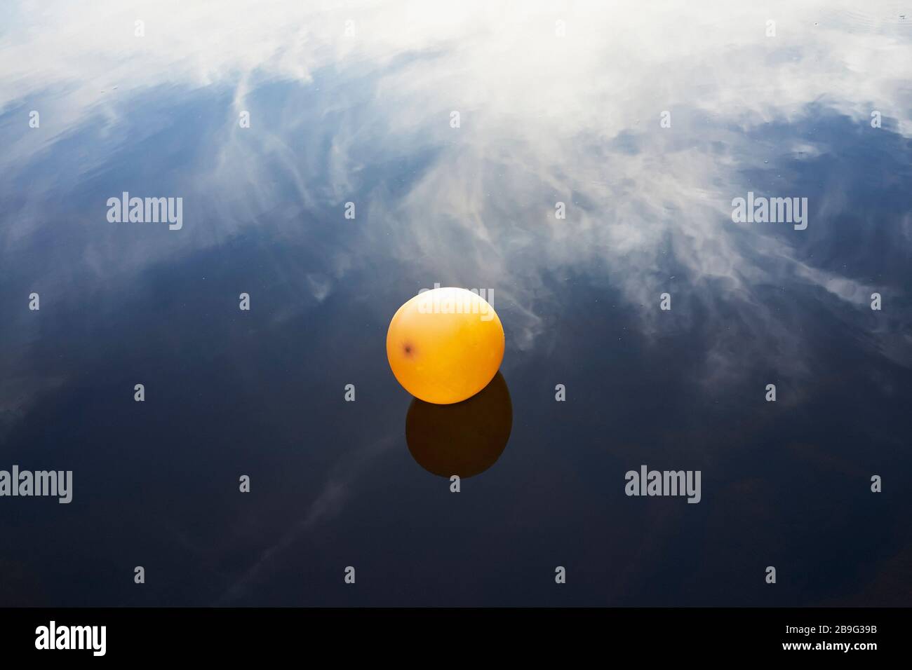 Yellow balloon floating on placid water reflecting clouds Stock Photo ...