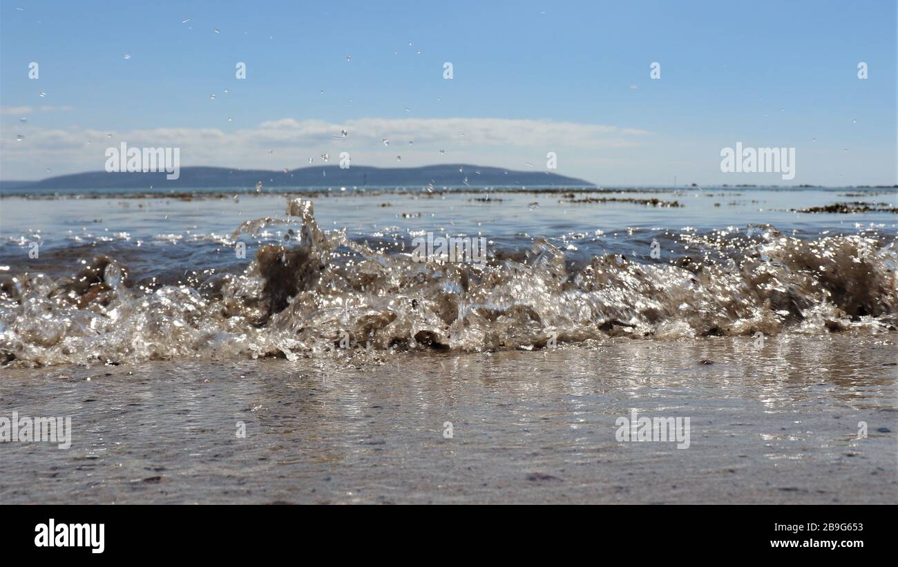 wave crushing on the beach, close up, mountains at the back, very hazy ...