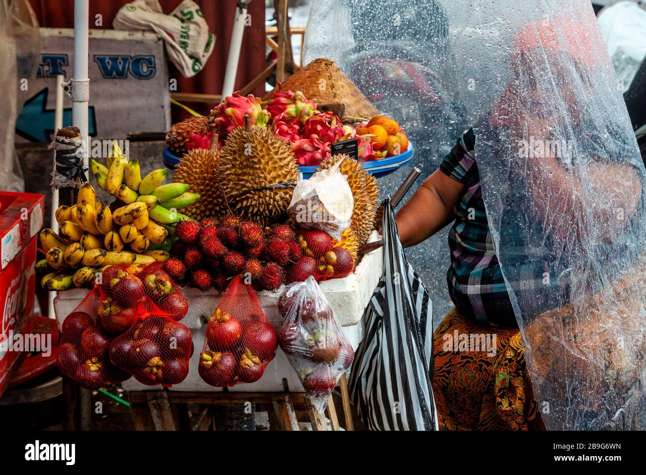 A Shop Owner Sits Under A Plastic Sheet During A Rain Shower Selling ...