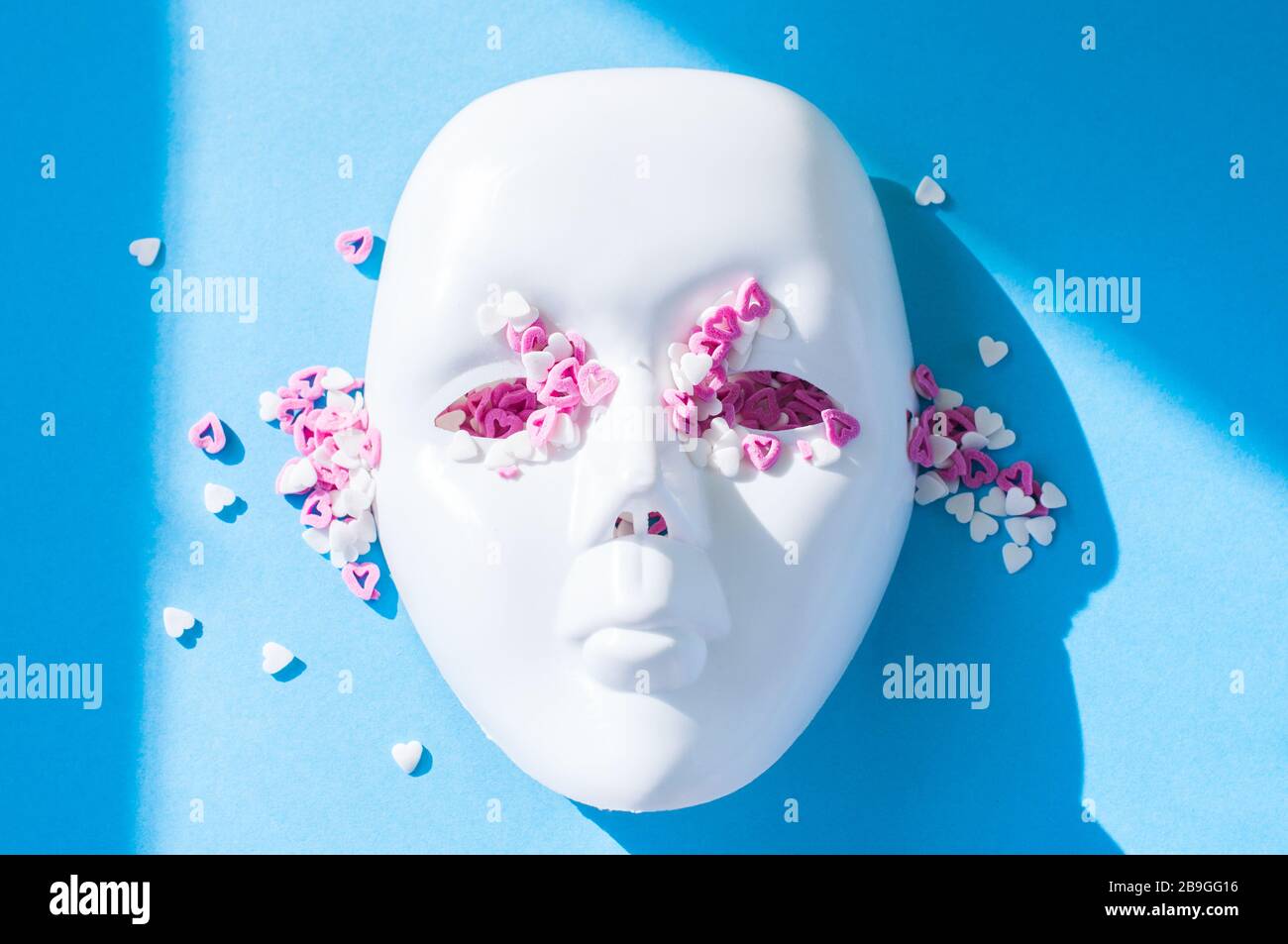 White plastic face mask with heart shaped sprinkles on a blue ...