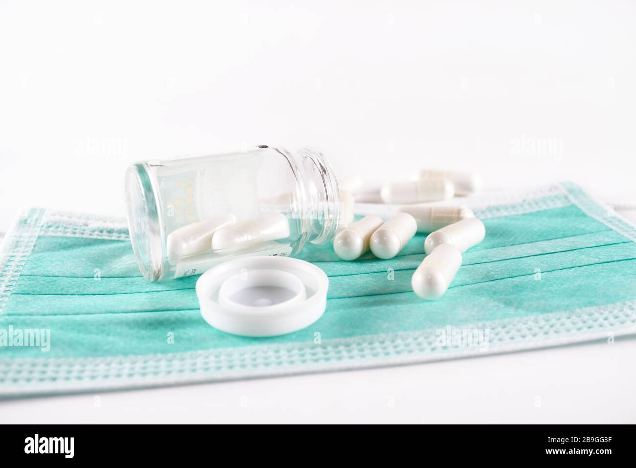 White medicine capsules spilling out of glass bottle on top of a ...