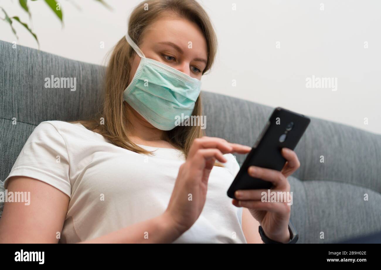 Woman in medical mask using mobile phone. Isolation at home Stock Photo ...