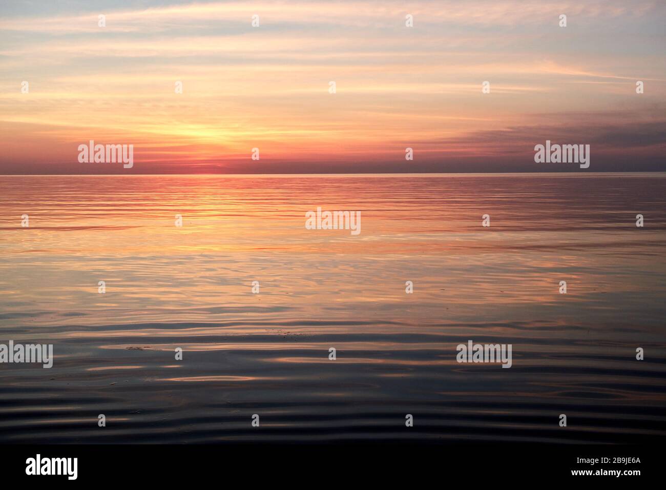 Sun over the water through clouds with straight ripples in water Stock ...