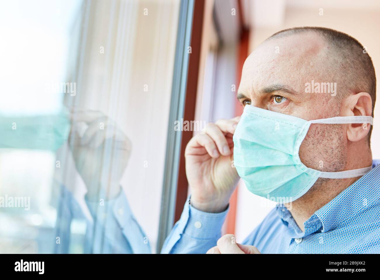 Covid-19 patient with quarantine face mask at home longingly looks out ...