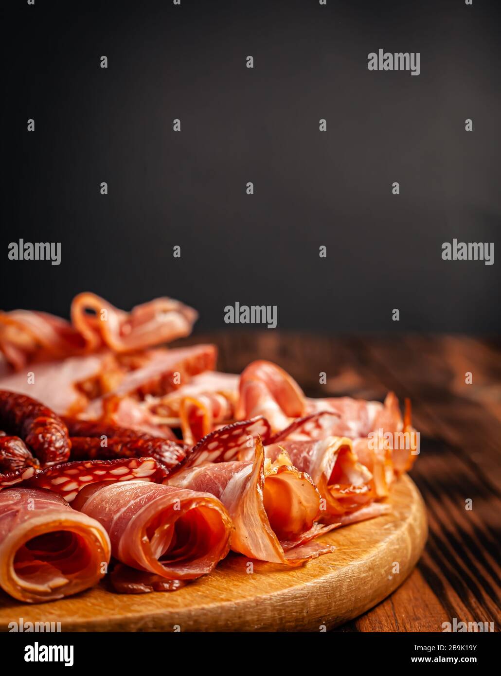 Assorted meat snacks on a wooden cutting board. Sausage, ham, bacon ...