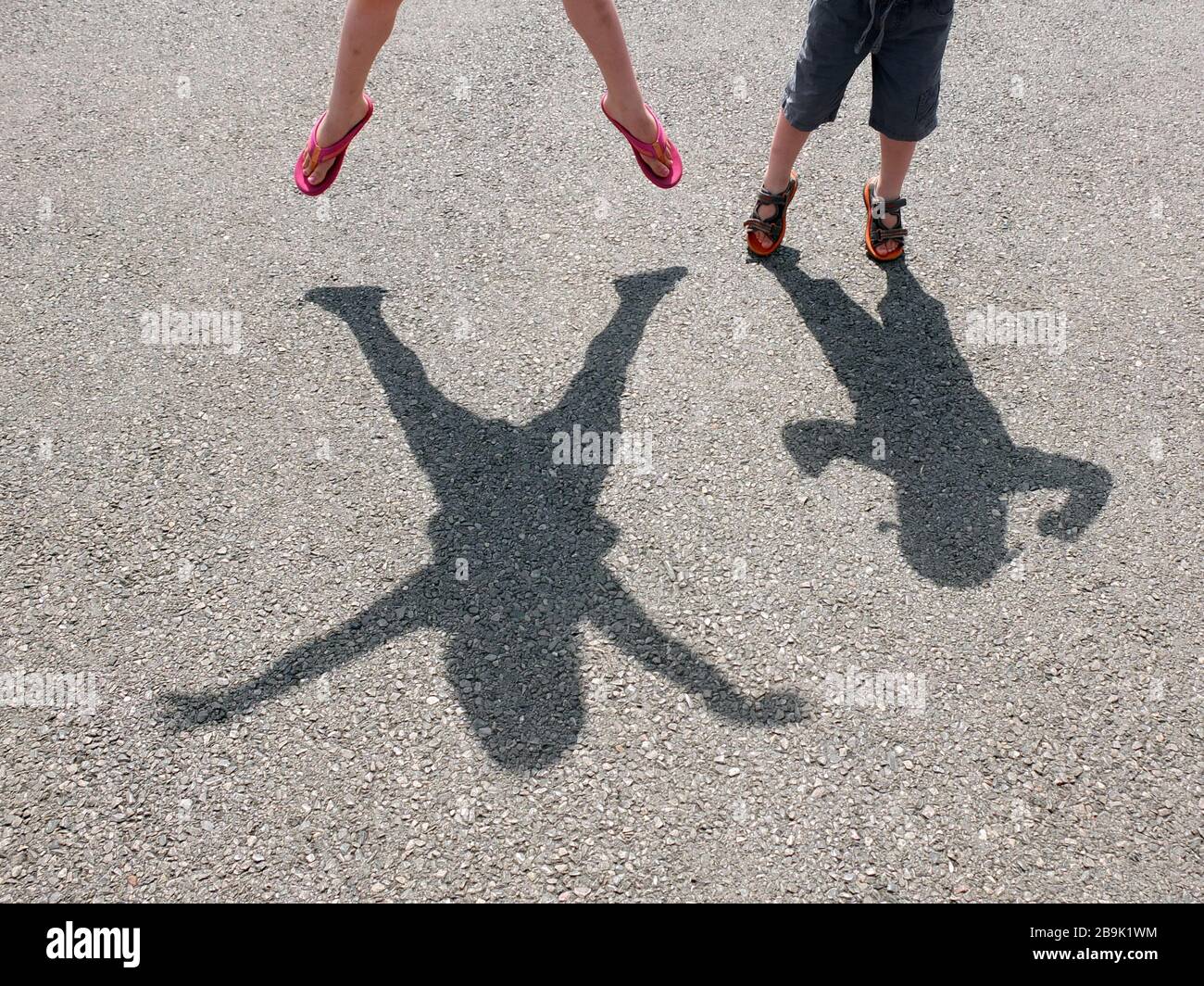 The shadows of two (2) young children on tarmac as they jump and play ...