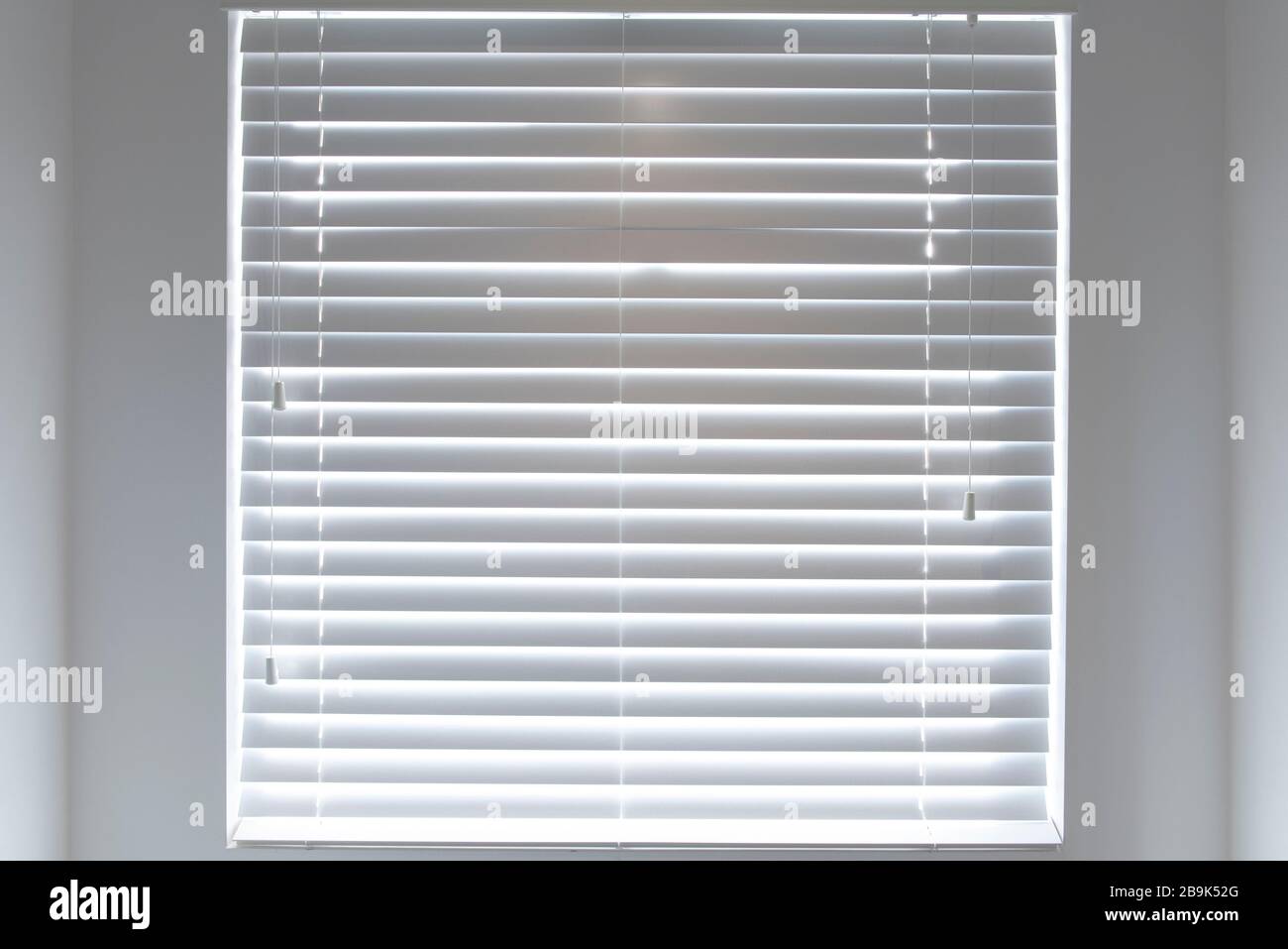 White slatted Venetian style wooden window blinds lowered during the ...