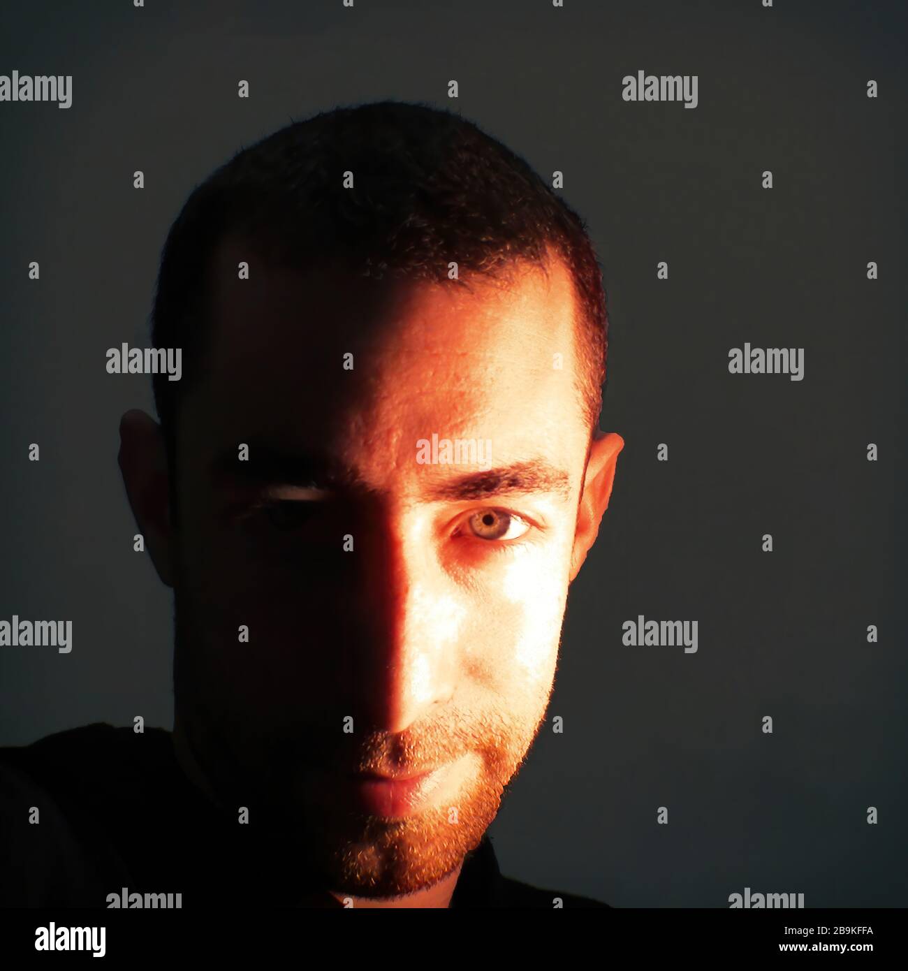 Bearded young man with a red light on his half-face looking at the ...