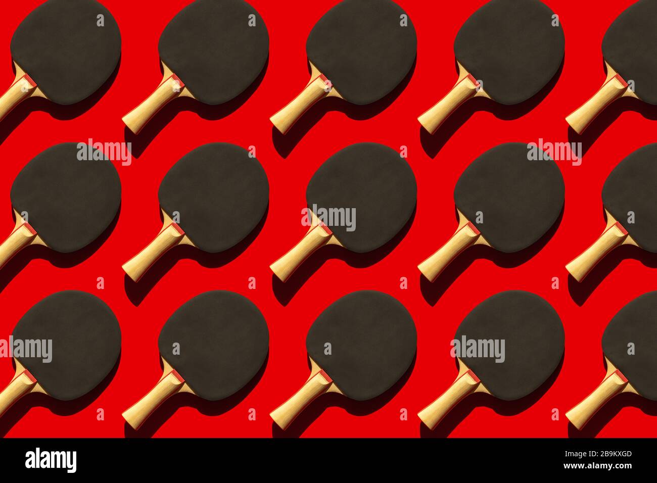 Repeating black tennis ping pong rackets with a hard shadow on a red ...
