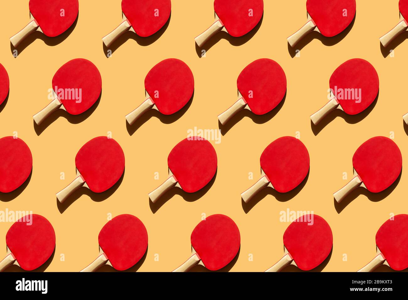 Repeating red tennis ping pong rackets with a hard shadow on a orange ...