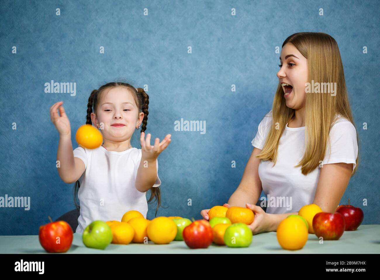 Little girl and mom play with fruits and fool around. They are wearing ...