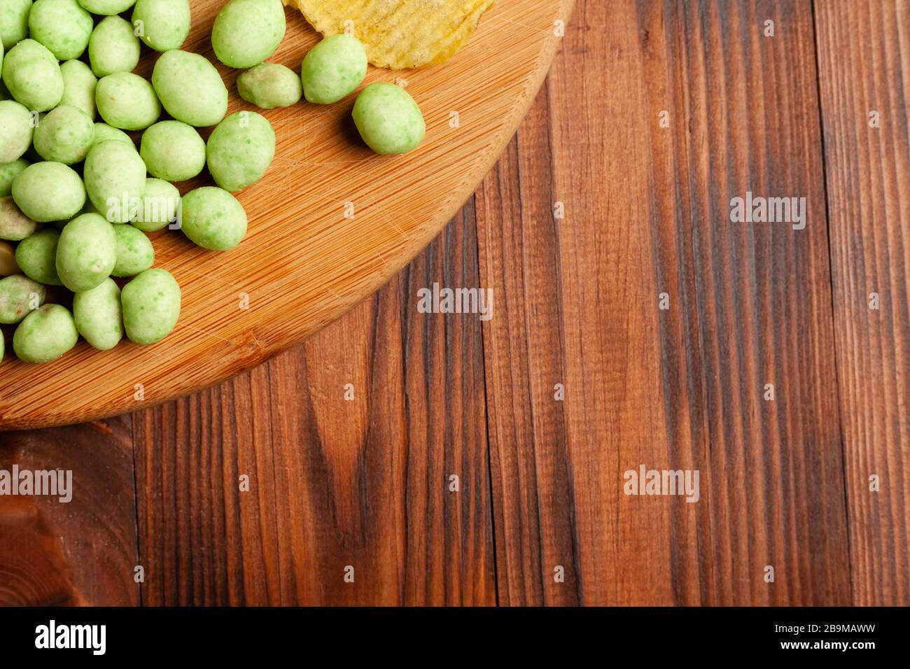 Assorted dry snacks on a wooden board. Chips, peanuts, croutons, wasabi ...