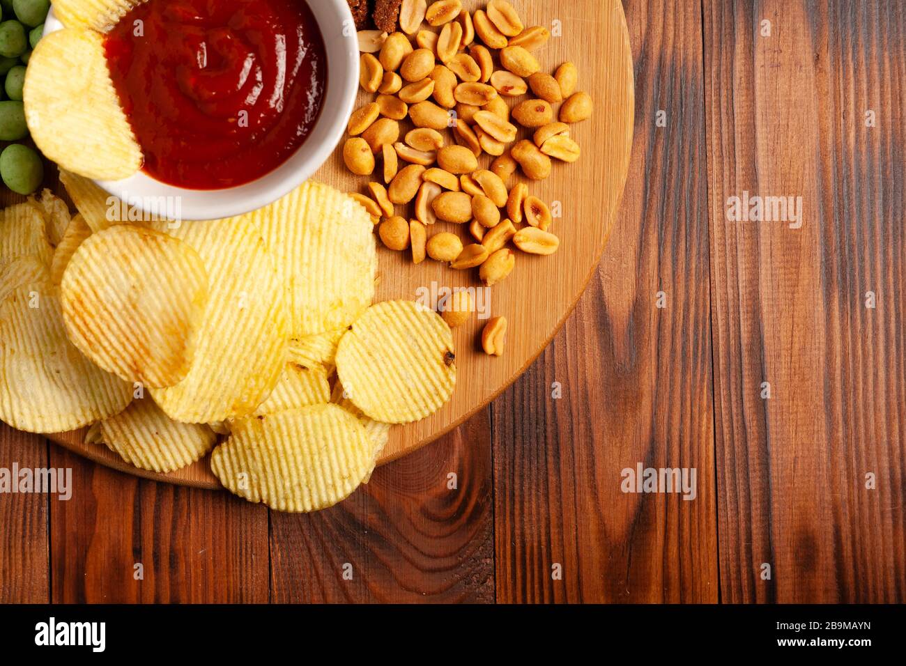 Assorted dry snacks on a wooden board. Chips, peanuts, croutons, wasabi ...