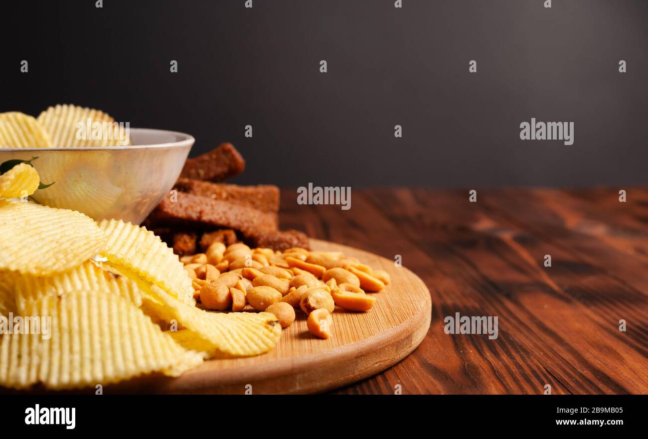 Assorted dry snacks on a wooden board. Chips, peanuts, croutons, wasabi ...