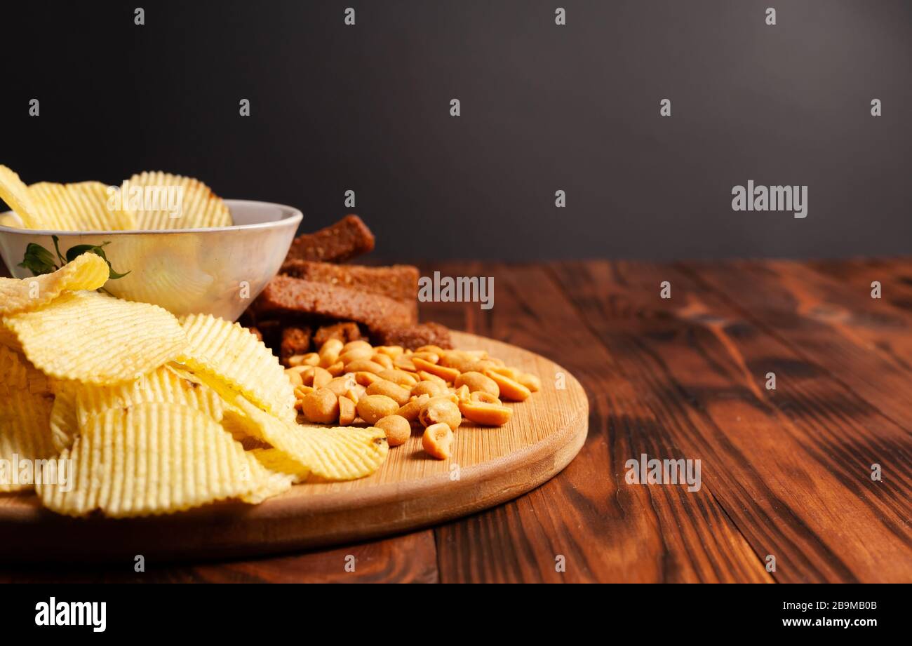 Assorted dry snacks on a wooden board. Chips, peanuts, croutons, wasabi ...