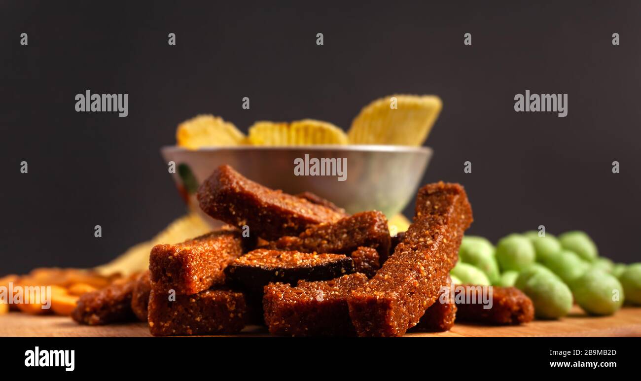 Assorted dry snacks on a wooden board. Chips, peanuts, croutons, wasabi ...