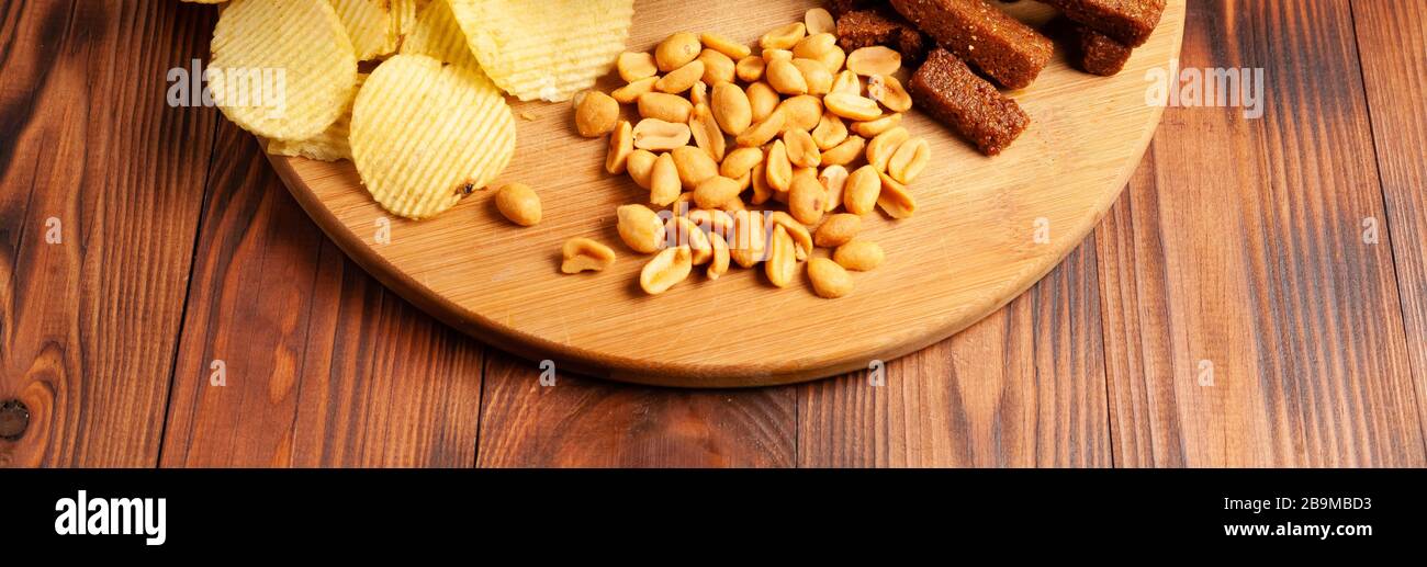 Assorted dry snacks on a wooden board. Chips, peanuts, croutons, wasabi ...