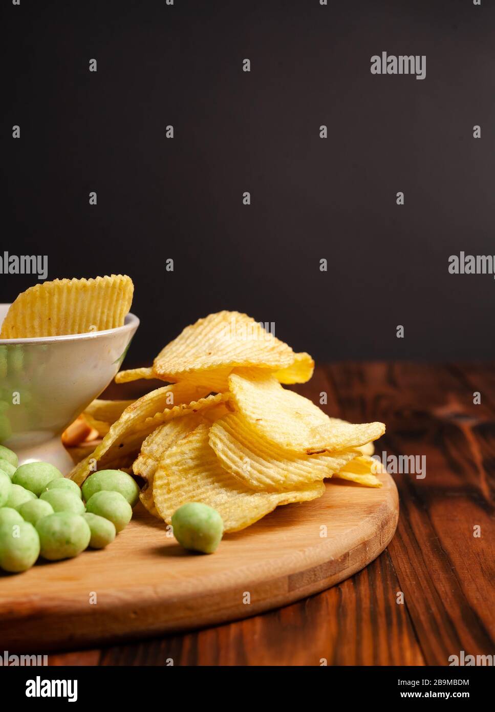 Assorted dry snacks on a wooden board. Chips, peanuts, croutons, wasabi ...