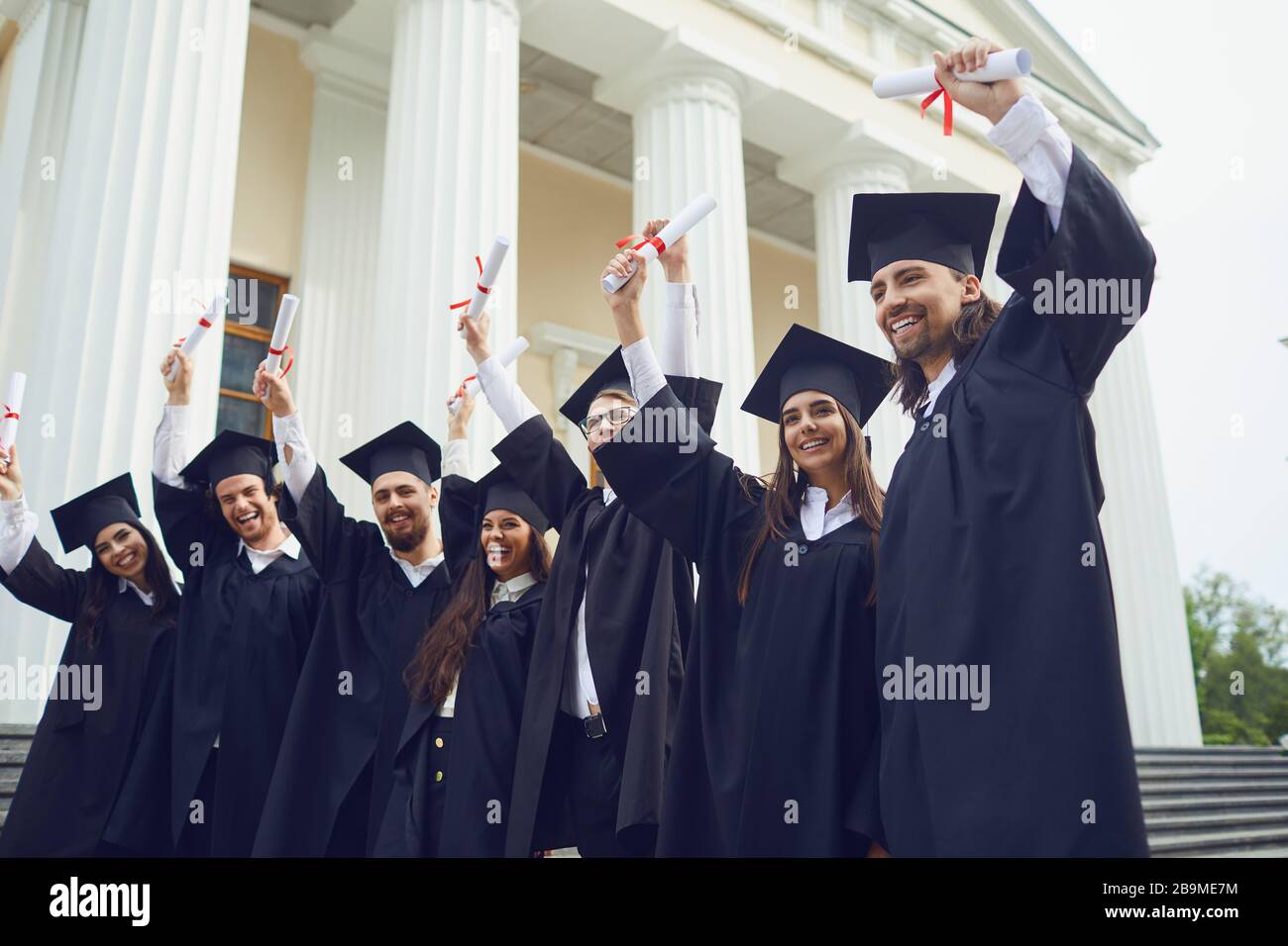 A group of graduate students raised their hands with diplomas up Stock ...