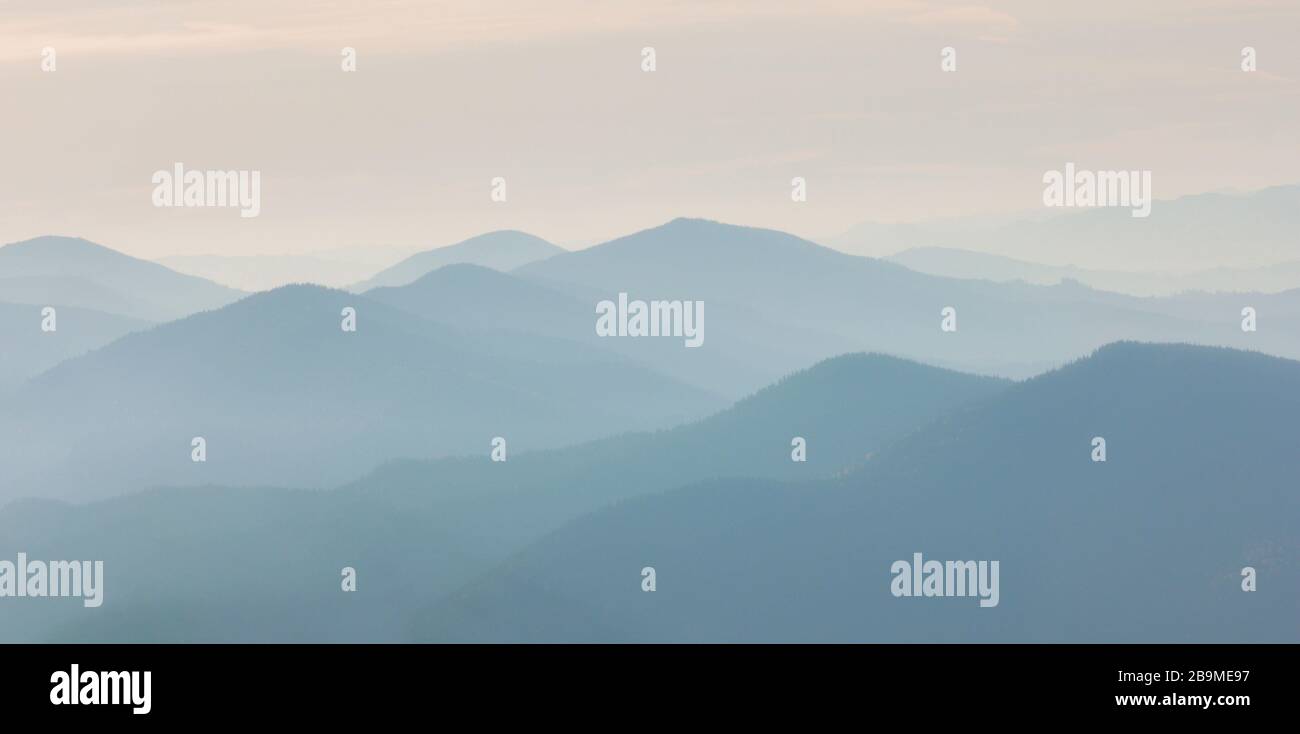 Warm gradient of dawn sky above layers of mountain and rock silhouettes ...