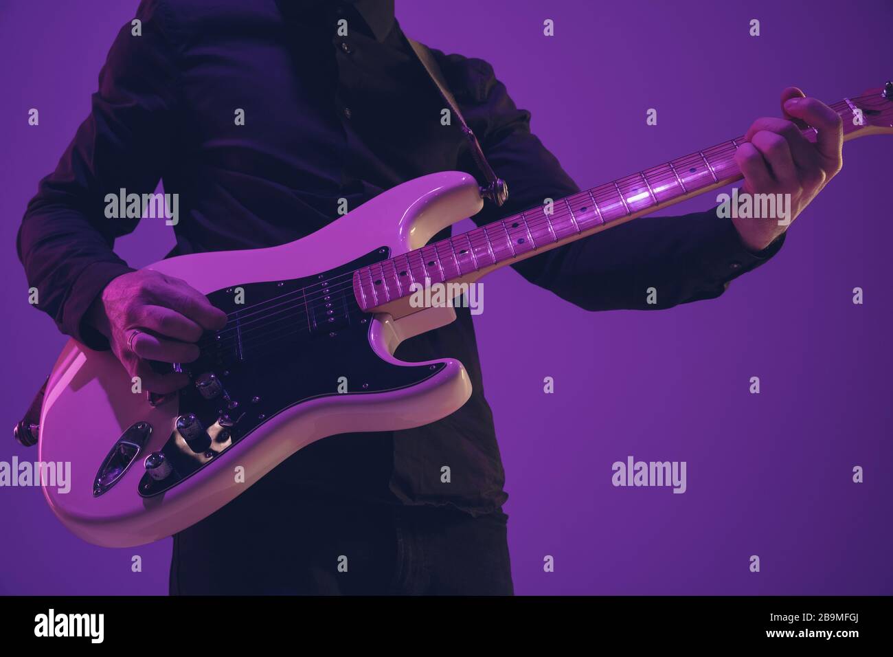 Young and joyful caucasian musician playing guitar on gradient purple ...