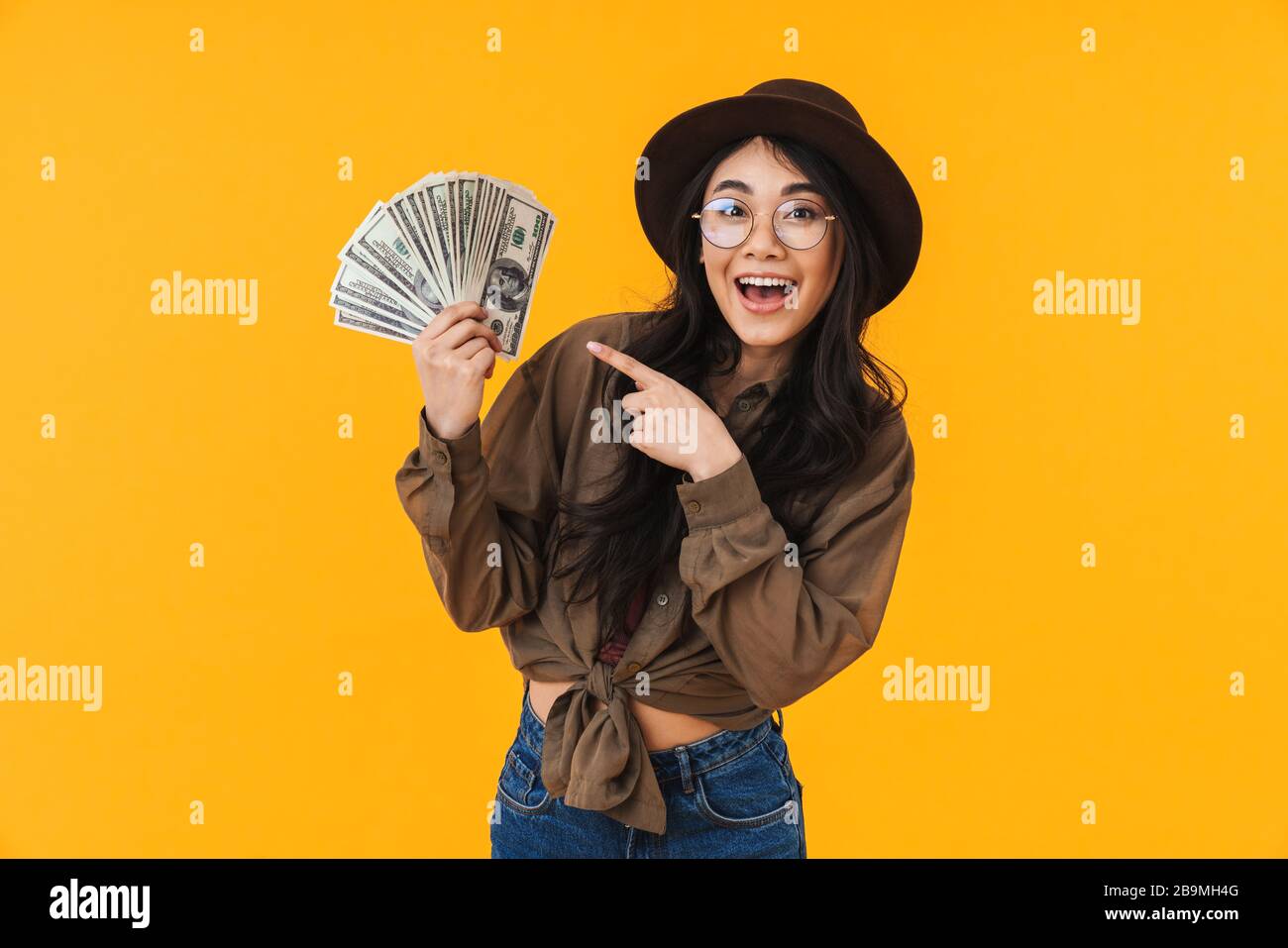Excited young asian woman showing money banknotes while standing ...