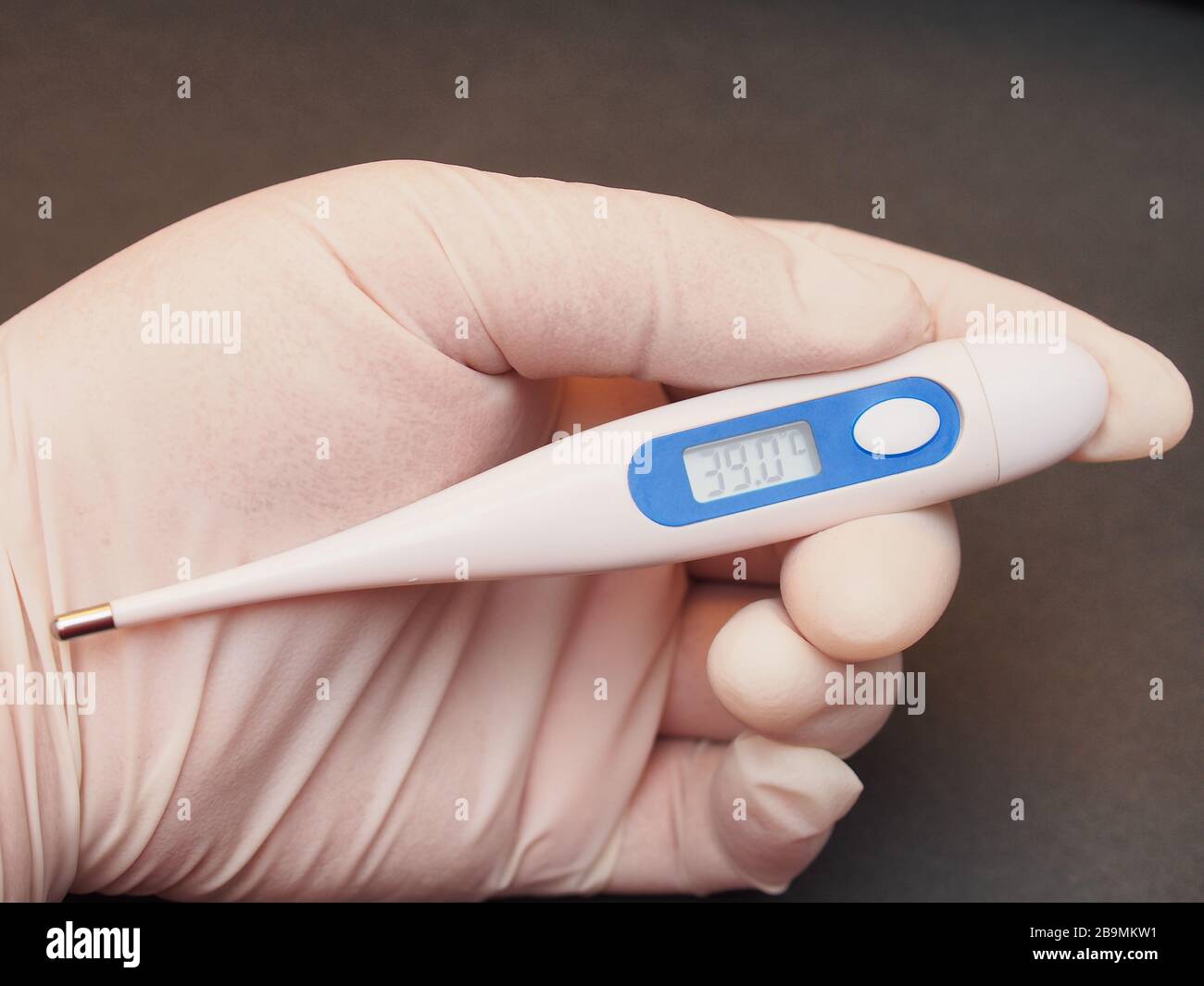 The electronic thermometer is held by a hand in a medical rubber glove ...