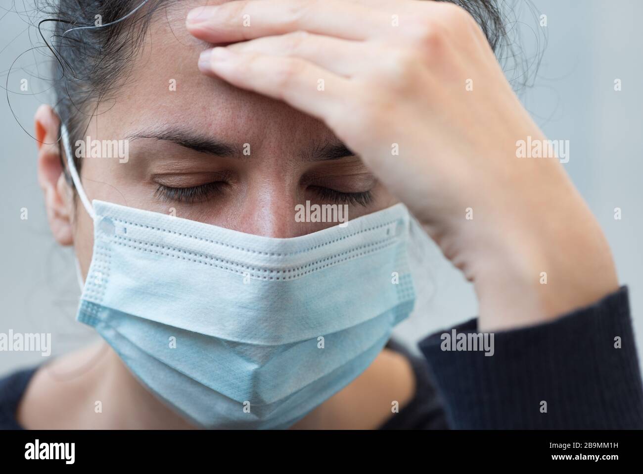 Close-up woman wearing a face surgical mask holding her head and having ...
