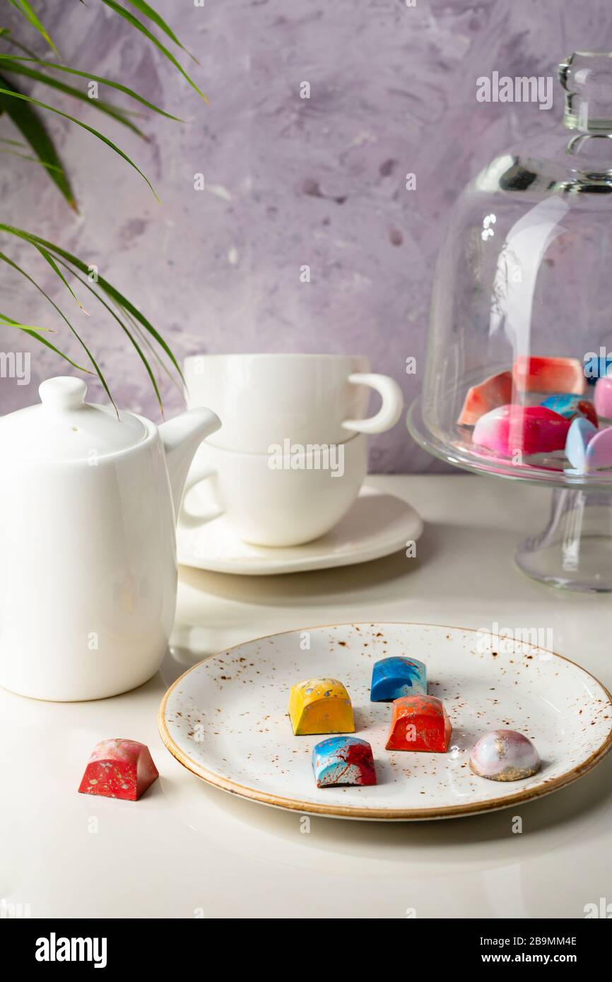 Modern chocolate candy on white plate and white teapot Stock Photo - Alamy