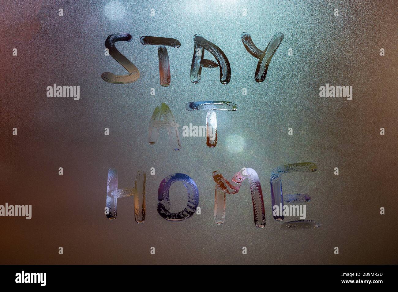 the words stay at home handwritten on wet window glass at night - close ...