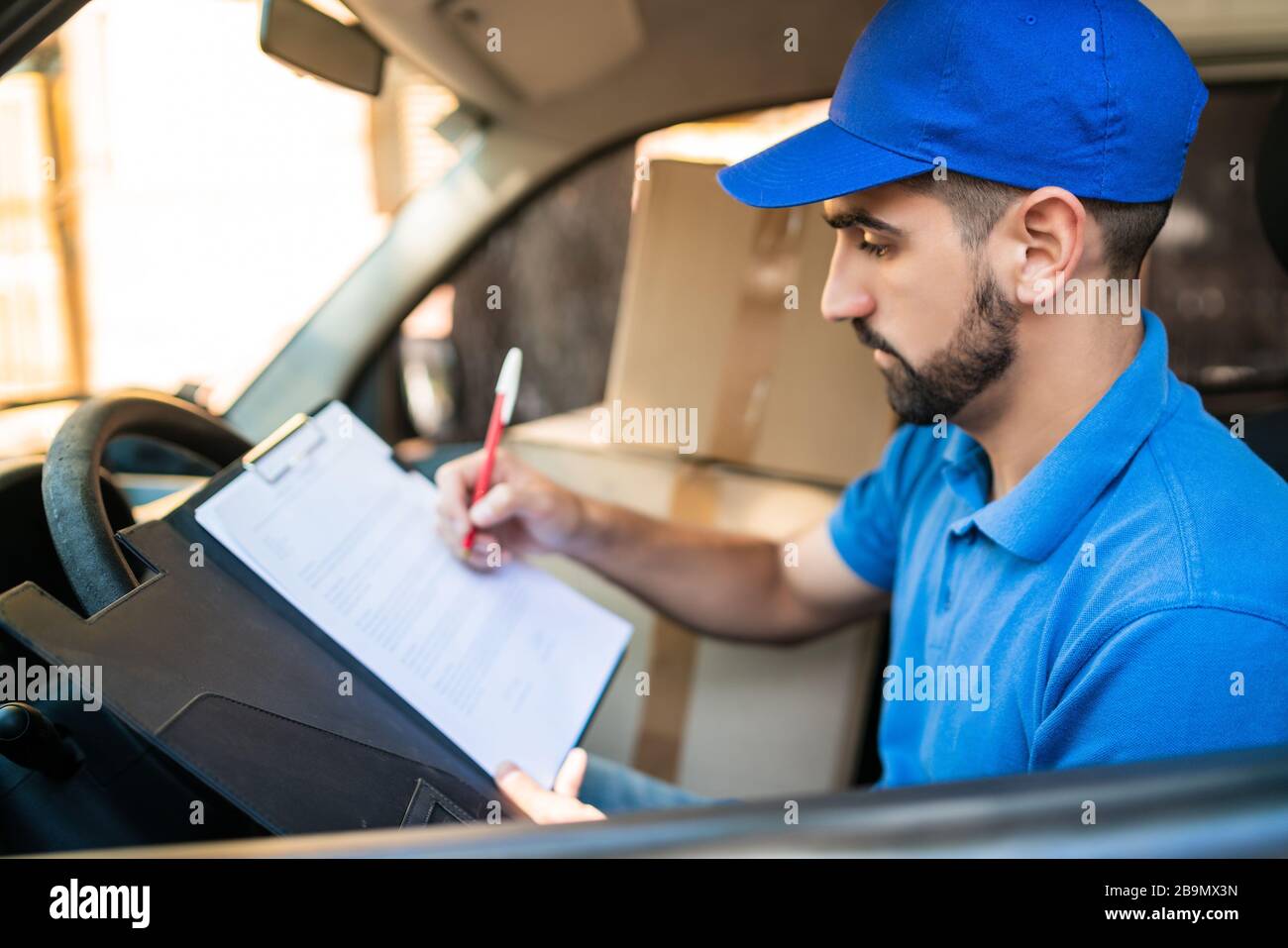 Portrait of a delivery man checking the delivery list while sitting in ...