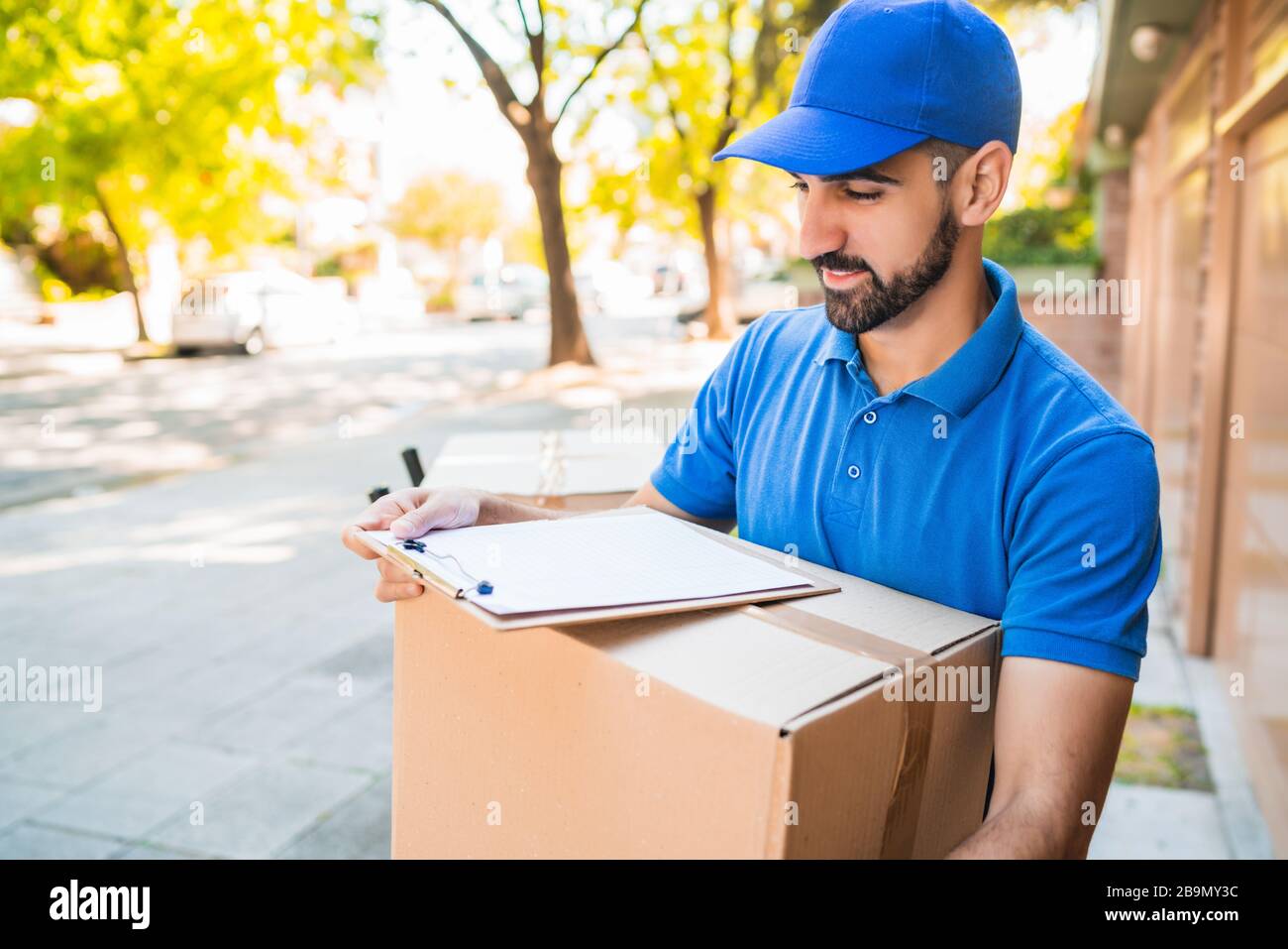 Portrait of a delivery man carrying cardboard boxes and checking list ...