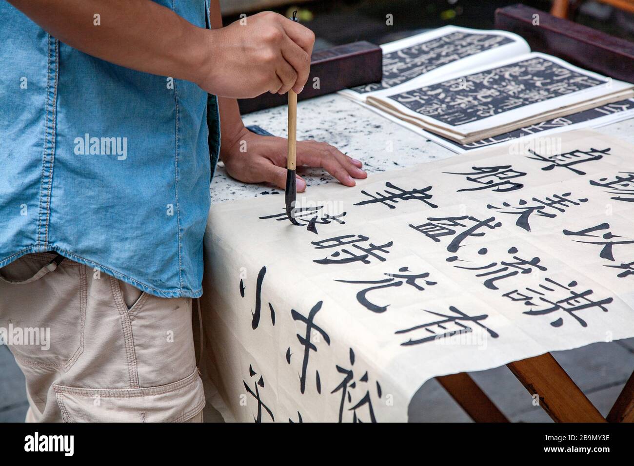 Chinese man writing large characters on sheet with paintbrush in ...