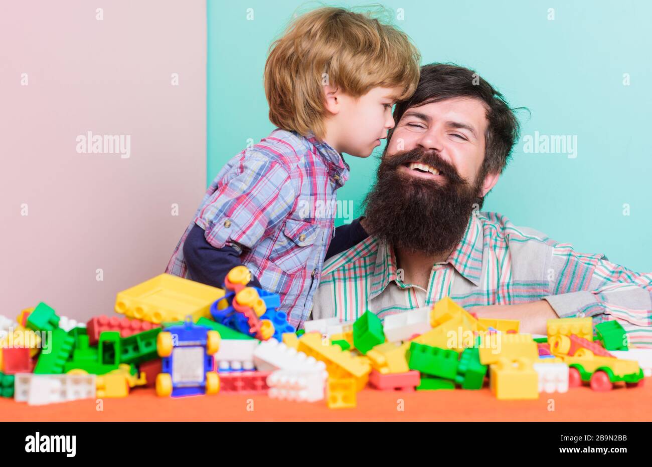 Bearded hipster and boy play together. Dad and child build of plastic blocks. Child care concept ...