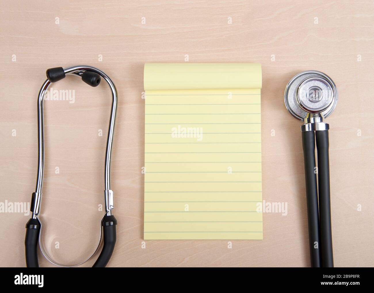Blank lined notepad on light wood table with stethoscope bell on one ...