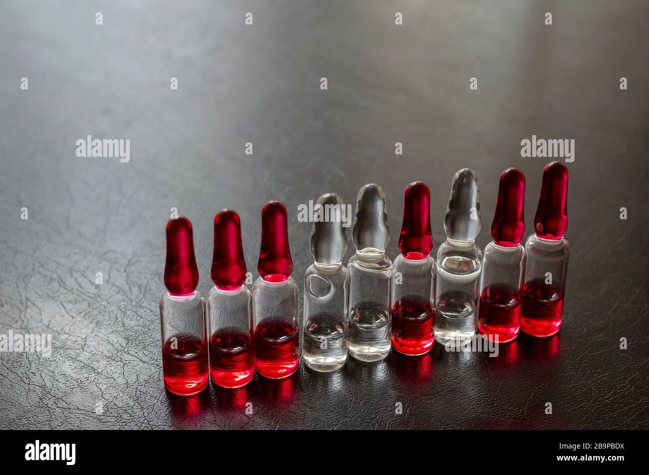 Red and colorless ampoules for injection on a dark background. Nine ...