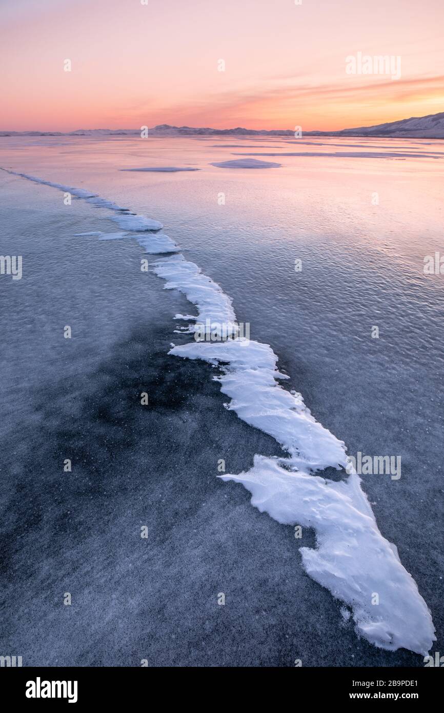 Frozen winter landscape of ice on lake Baikal during a colorful sunset ...