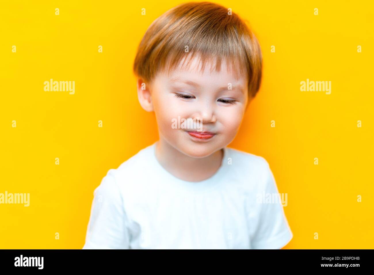 Shy small child three years old isolated on yellow background look down ...
