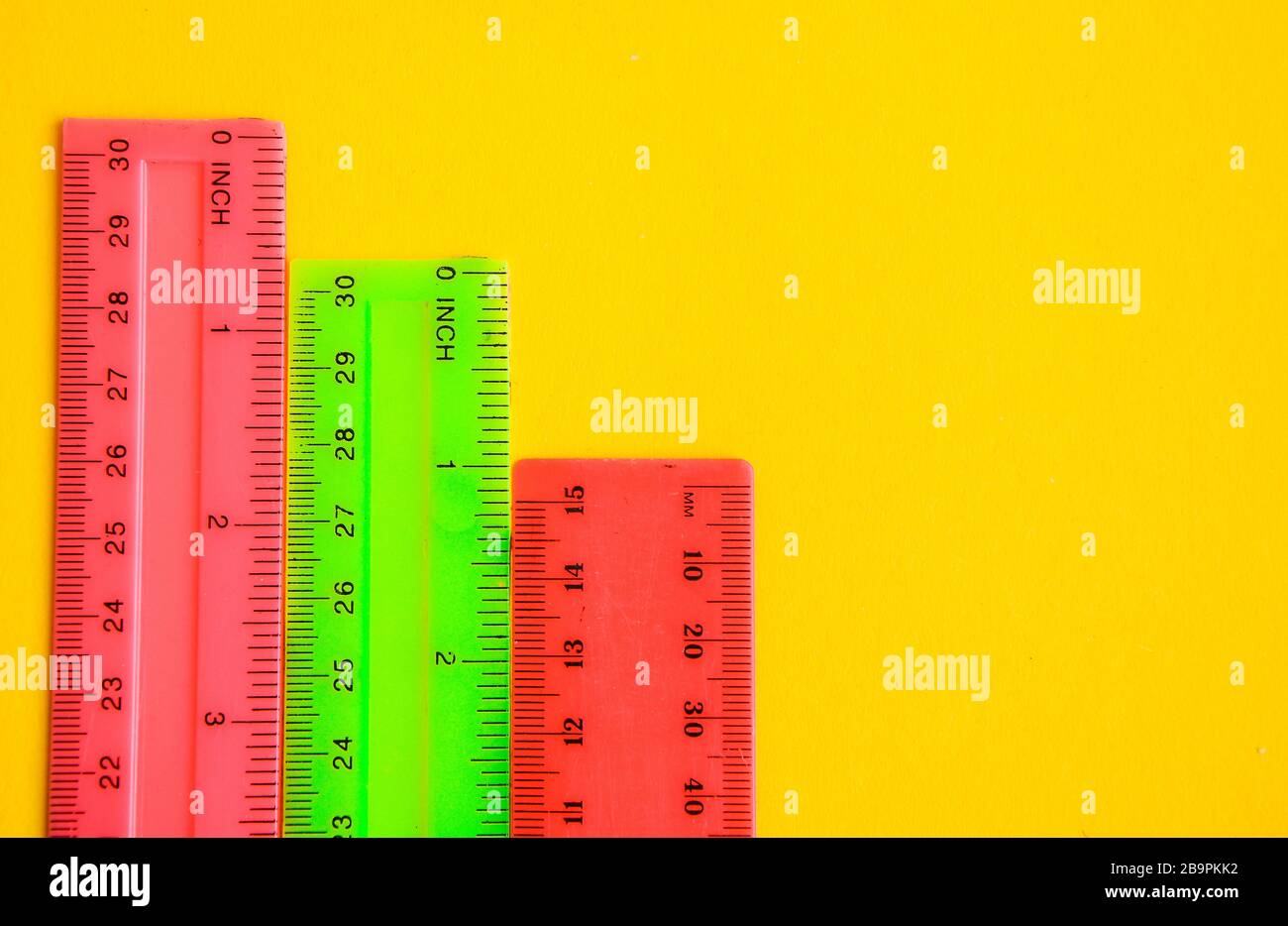 yellow and pink plastic rulers on yellow background with copy space ...