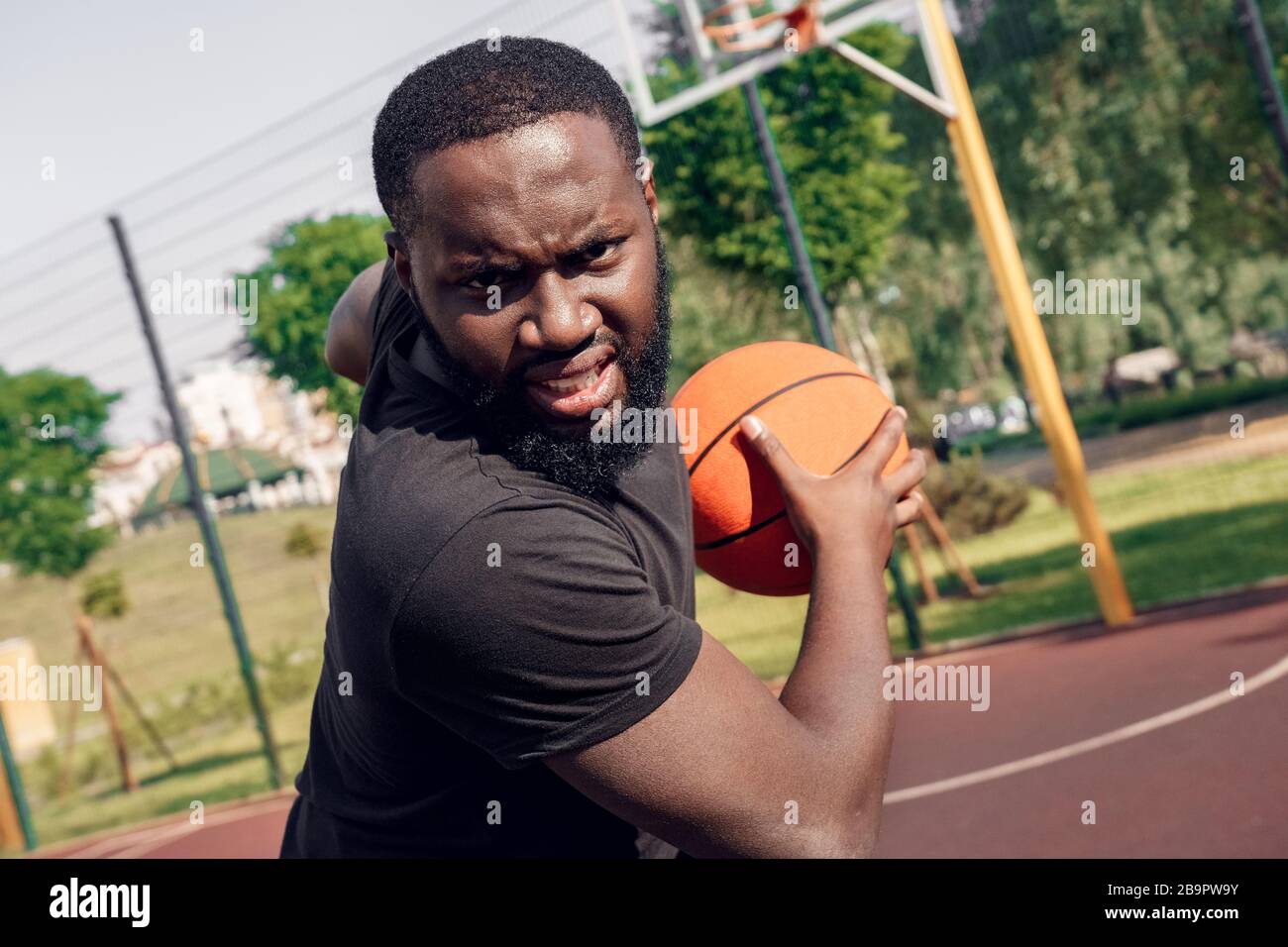 Outdoors Activity. African man running with ball on court angry close ...