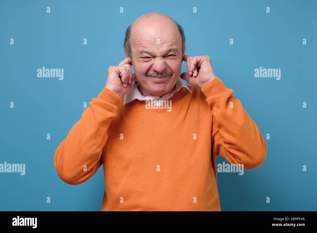 Mature man suffering from loud music and pain trying to plug ears Stock ...