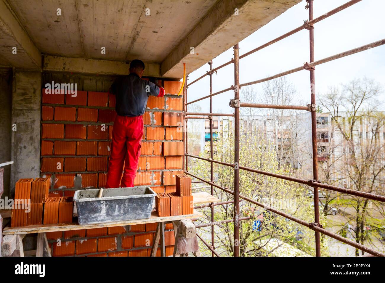 Mason, bricklayer worker is using red blocks to mount a wall at ...